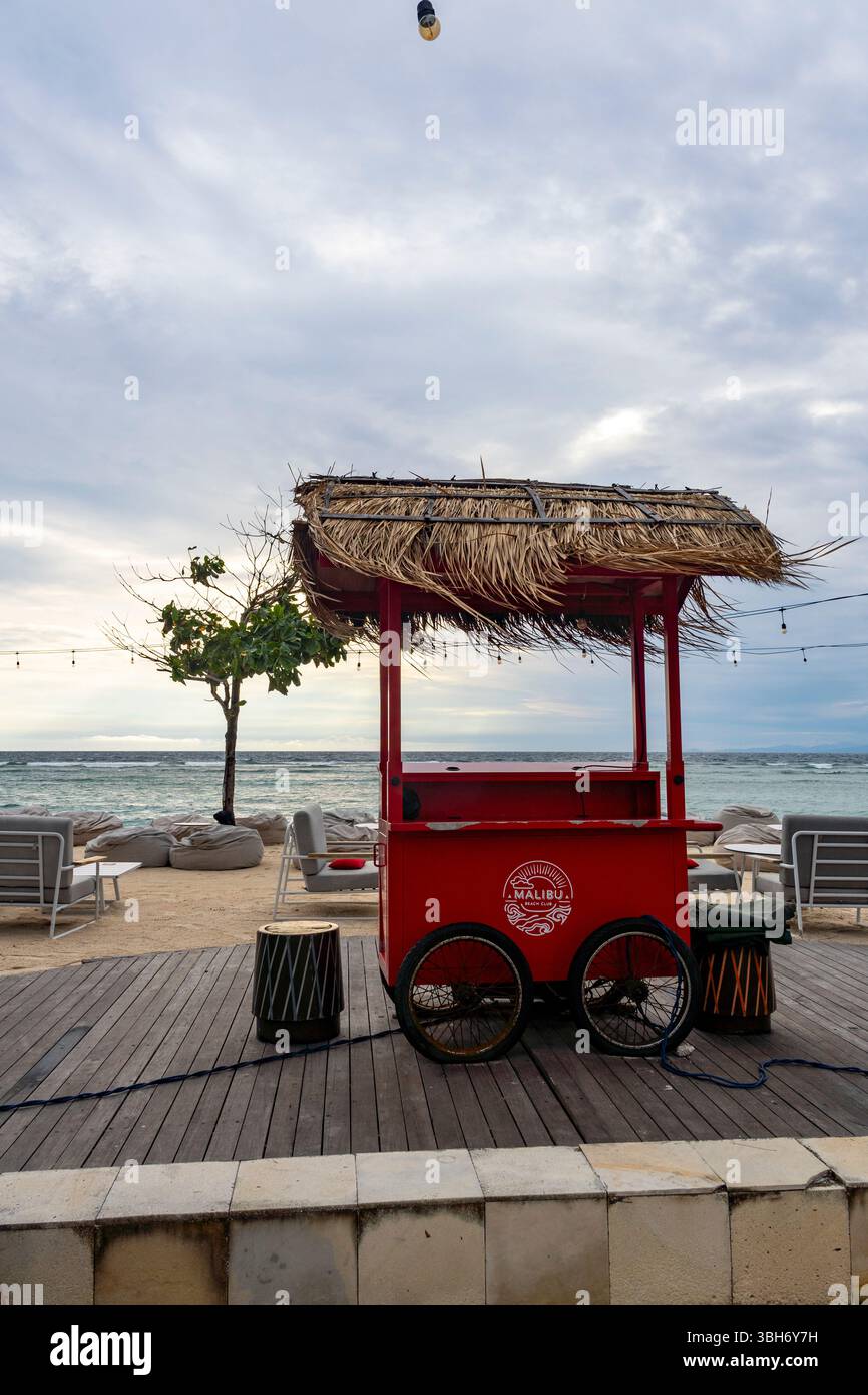 Beach scene with a red cart and umbrellas. The cart is red and has ...