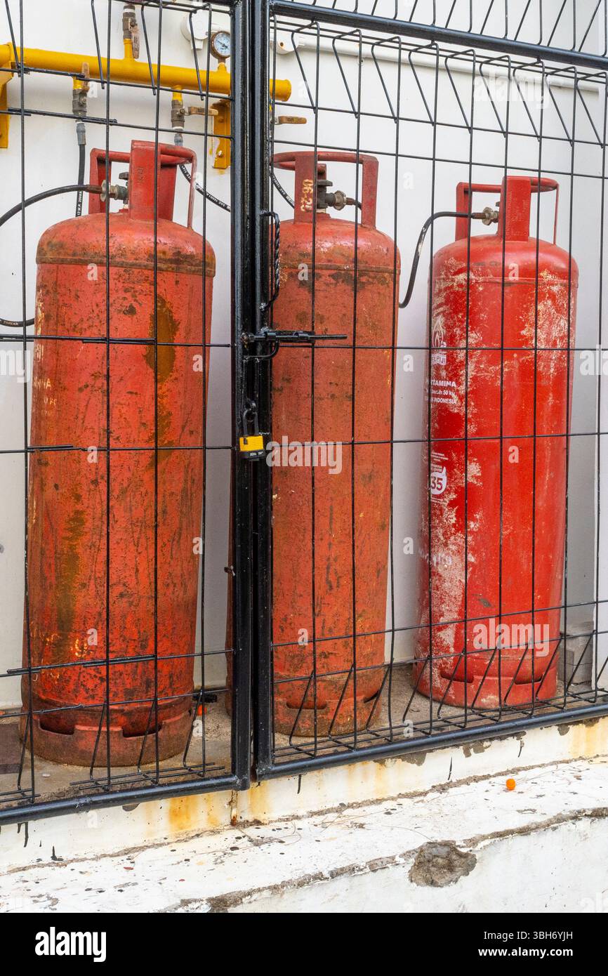 Four red gas tanks are chained to a wall. The tanks are rusty and old ...