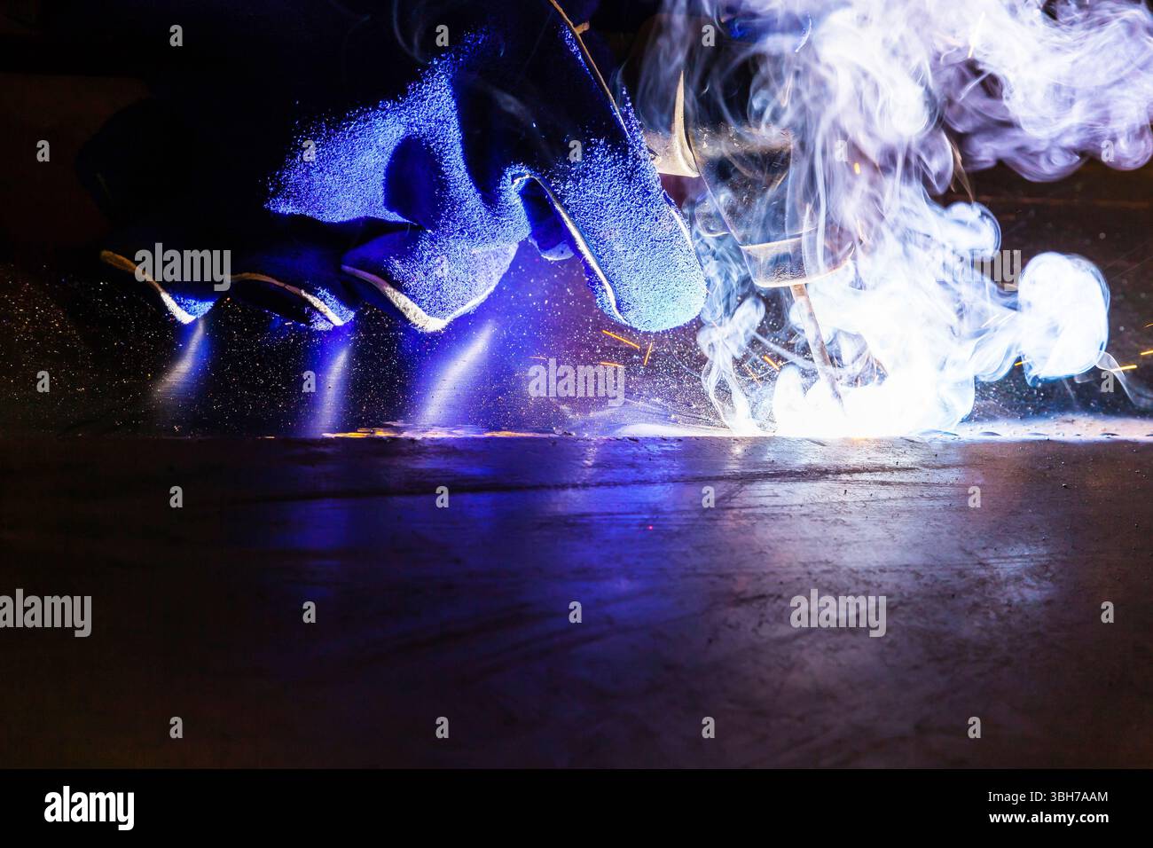 A welder in a welding mask and gloves welds with electric arc welding ...