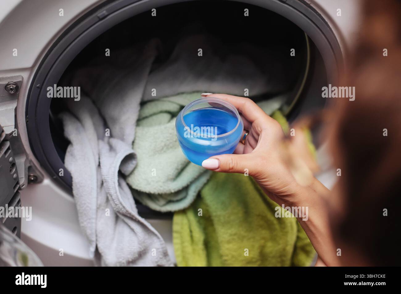 Pouring liquid fabric softener. Holding cap with blue conditioner near ...
