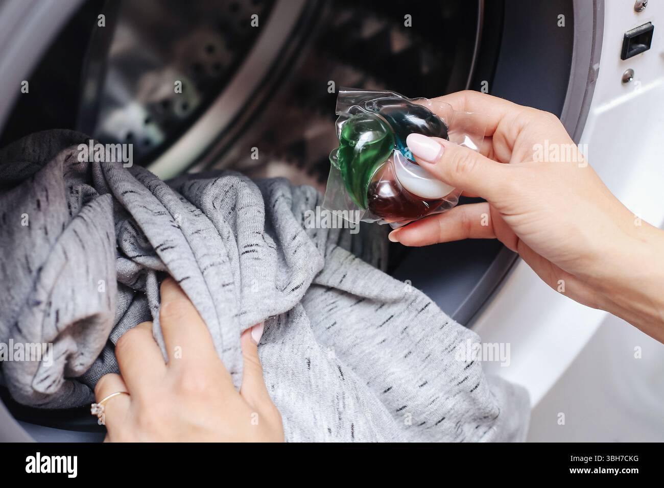 Laundry capsule in hand. Placing detergent pod into washing machine ...