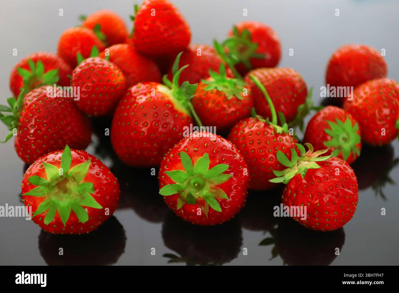 Heap of fresh red strawberries with green stems on a glossy black ...