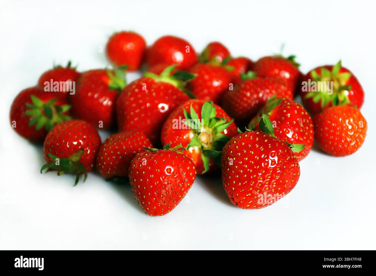 Pile of ripe red strawberries with green stems on a clean white ...