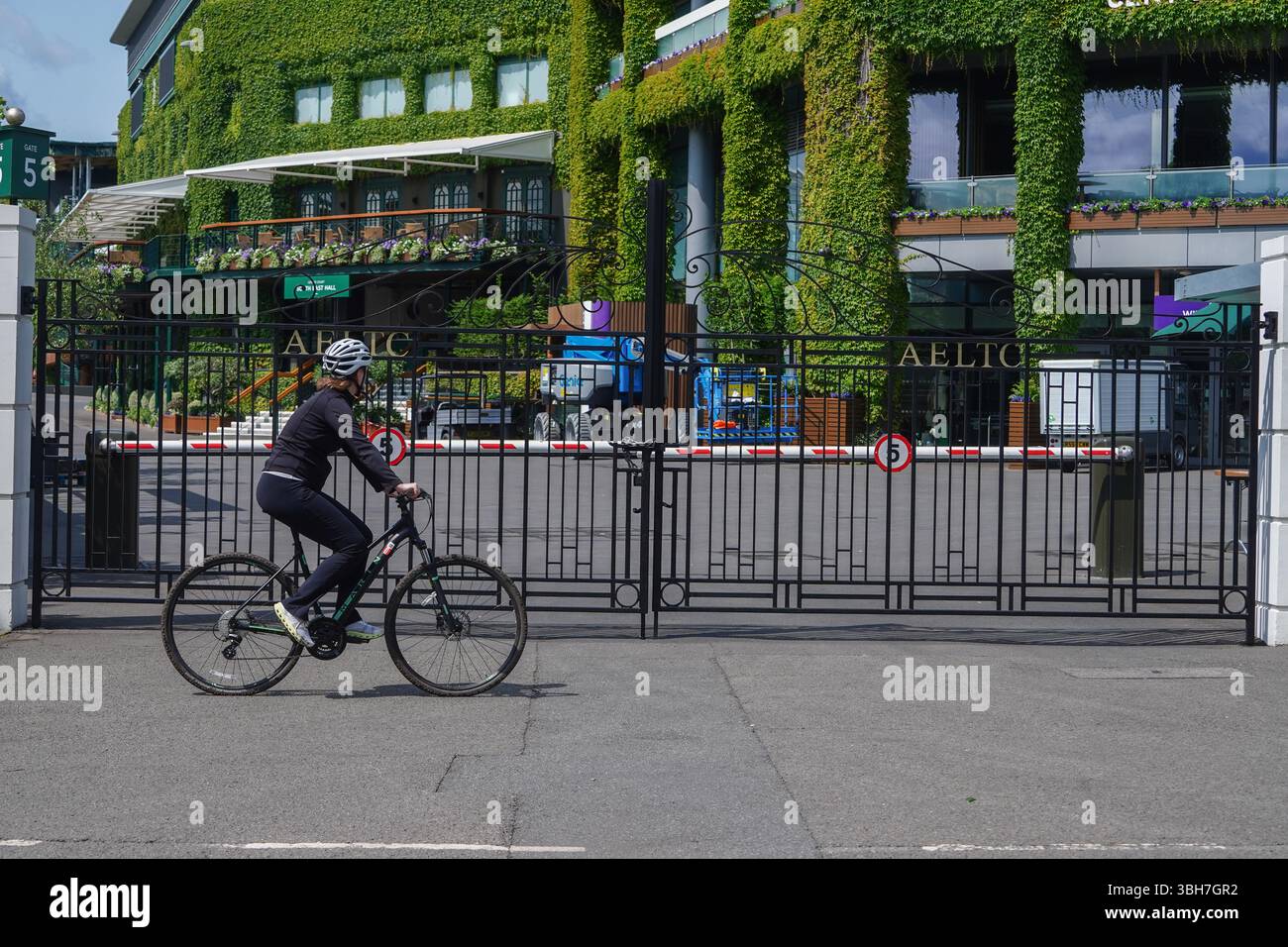 Wimbledon London, UK. 8 June 2025 A cyclist rides past the main gate of ...