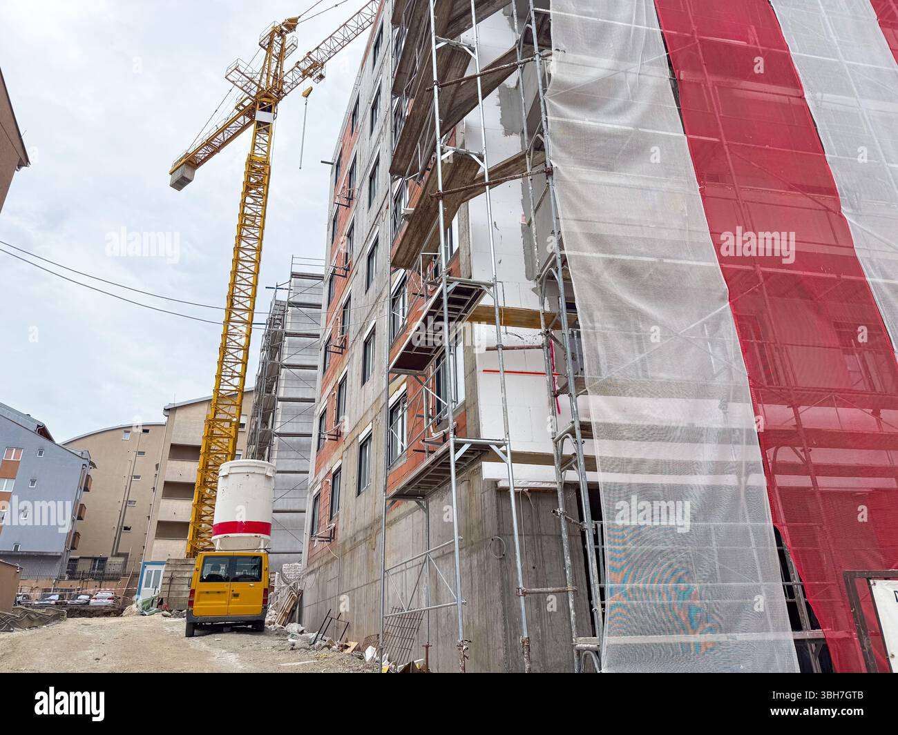 Yellow crane and scaffolding on urban building site. Protective mesh ...