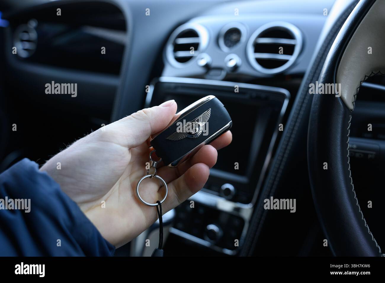 This image features a hand holding a Bentley key fob inside a luxury ...