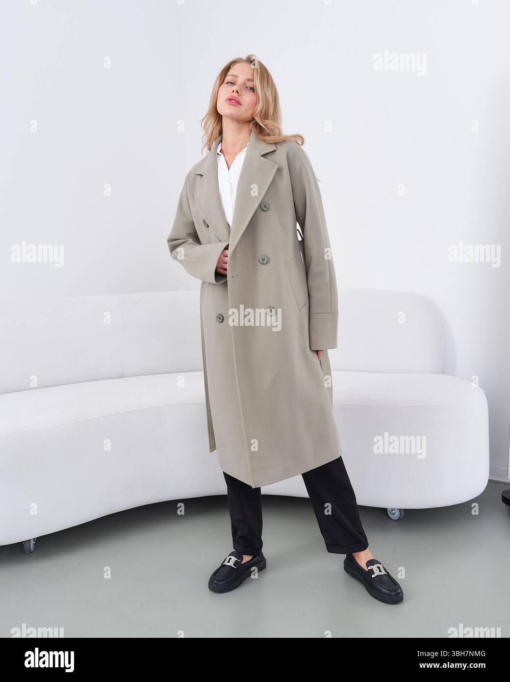 Woman wearing a stylish beige trench coat over a white shirt stands in ...