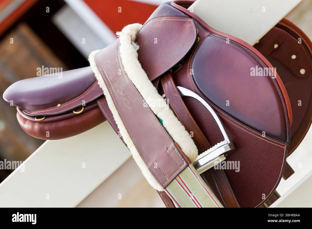 A close-up of a rider's stirrup and English saddle resting on a fence ...