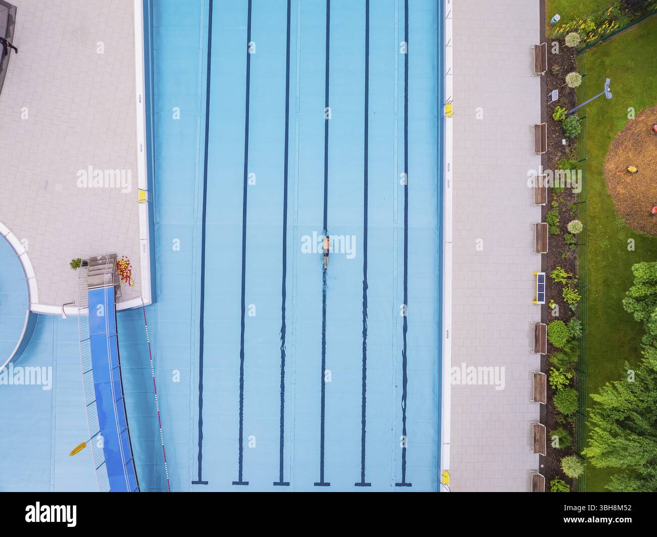 A swimmer swimming laps in a large swimming pool surrounded by green ...