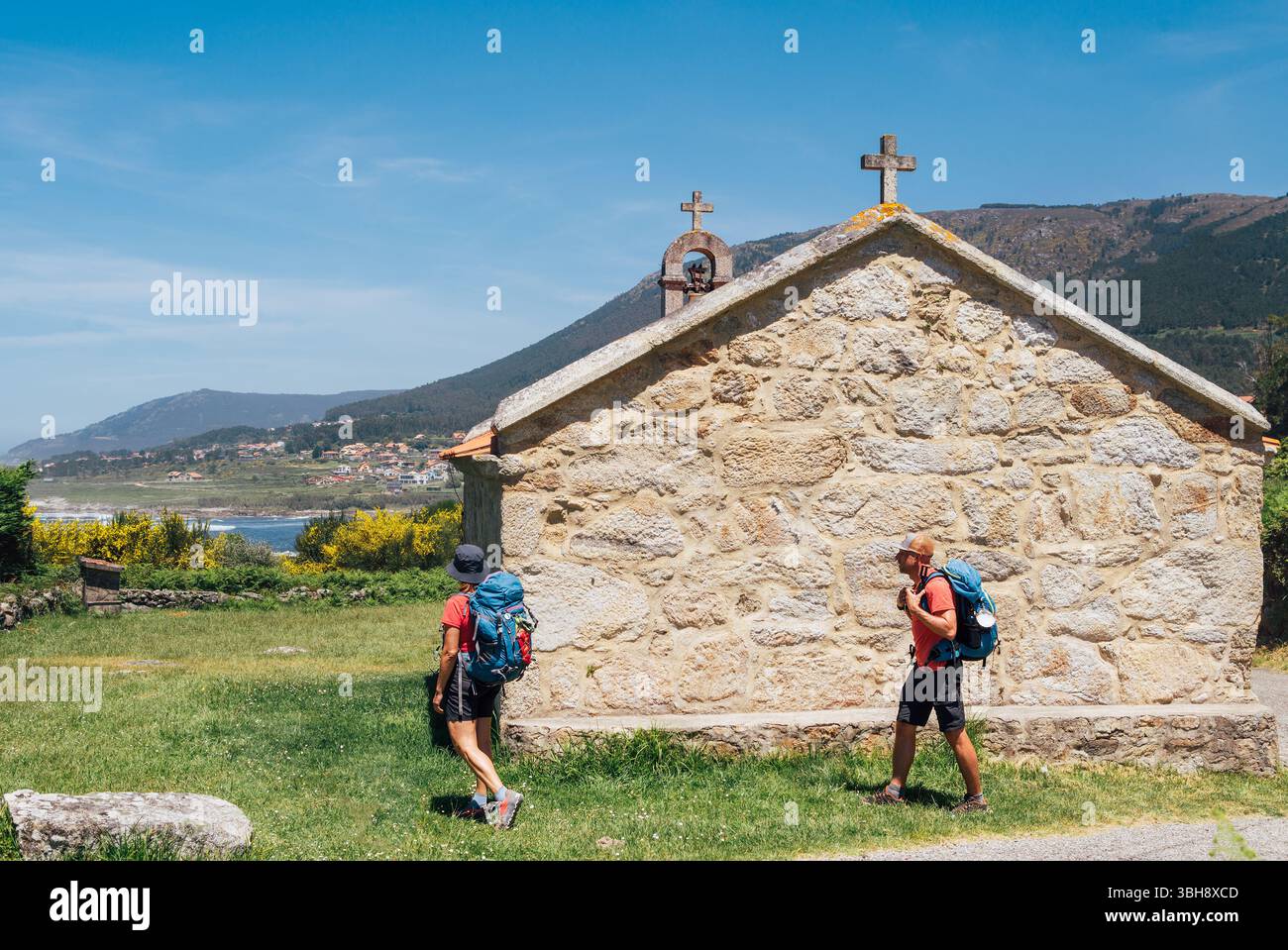 Couple of pilgrims with backpacks walking next to old church on Camino ...