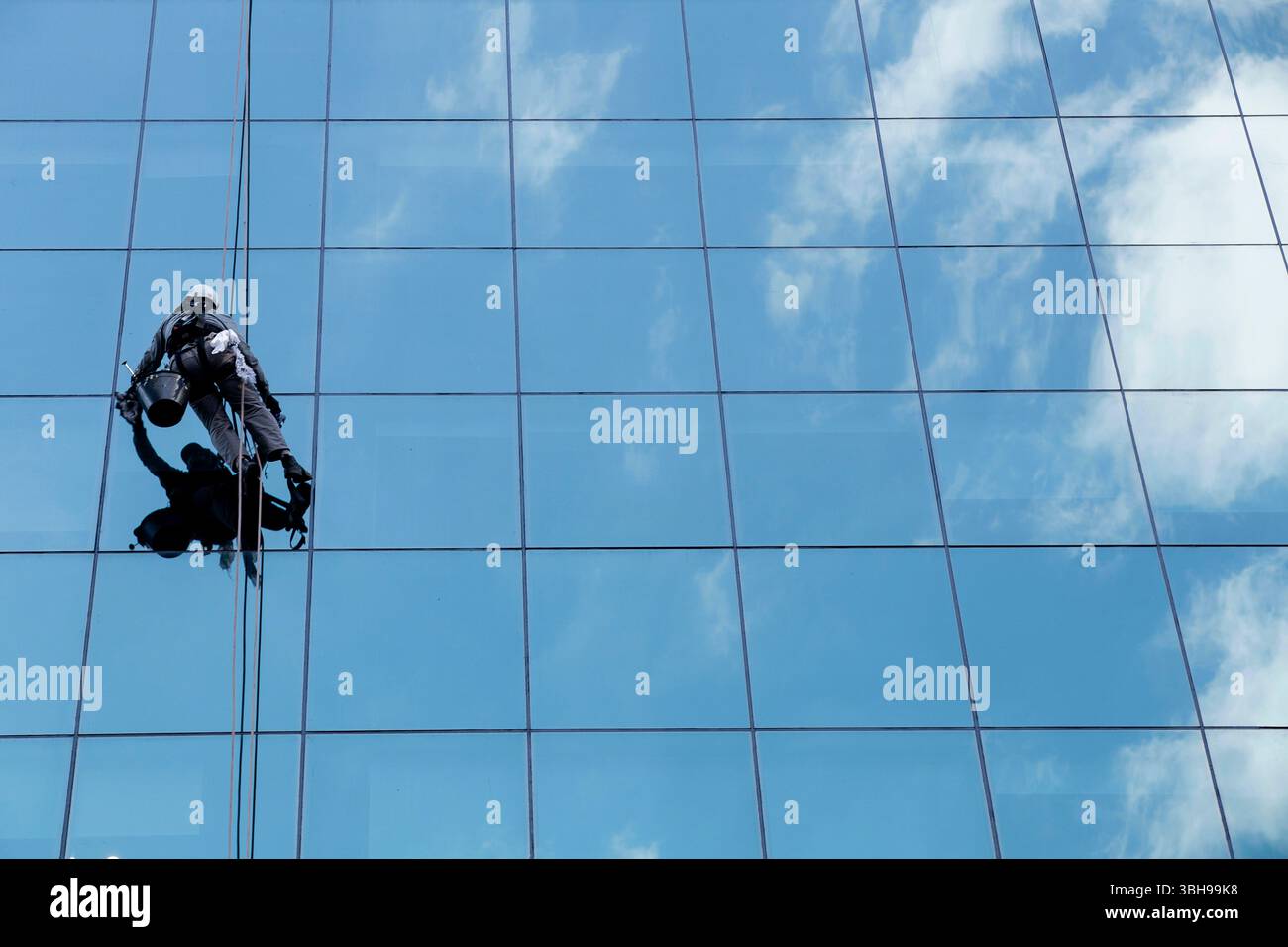 A worker cleaning mirrored windows with a reflection of the sky and clouds of a commercial ...