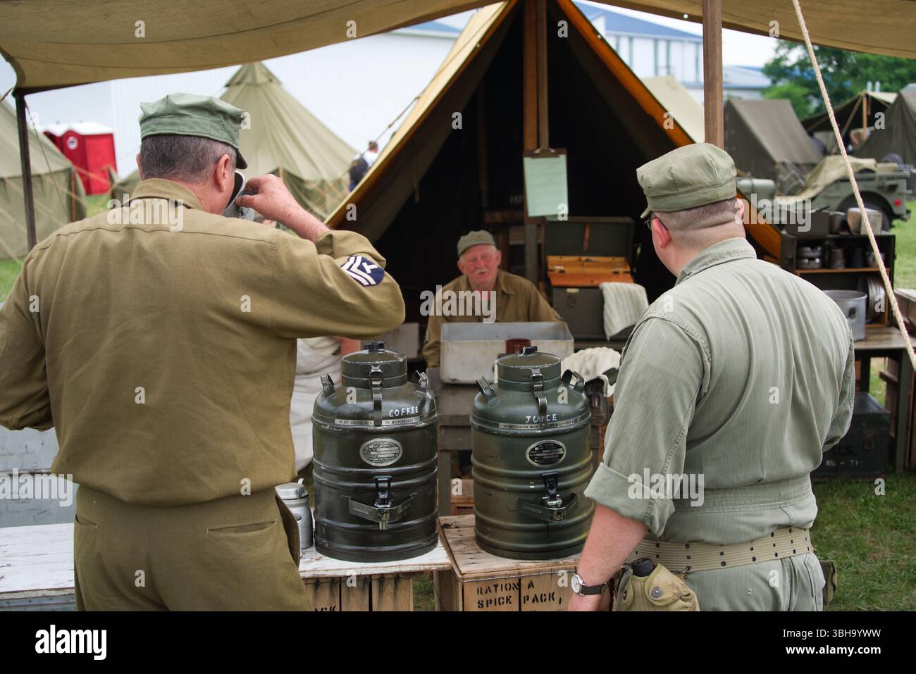 Three men in WWII-era military uniforms are standing near army-style ...