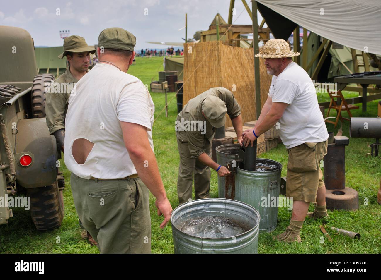 Several men in WWII-era military uniforms prepare water in metal ...