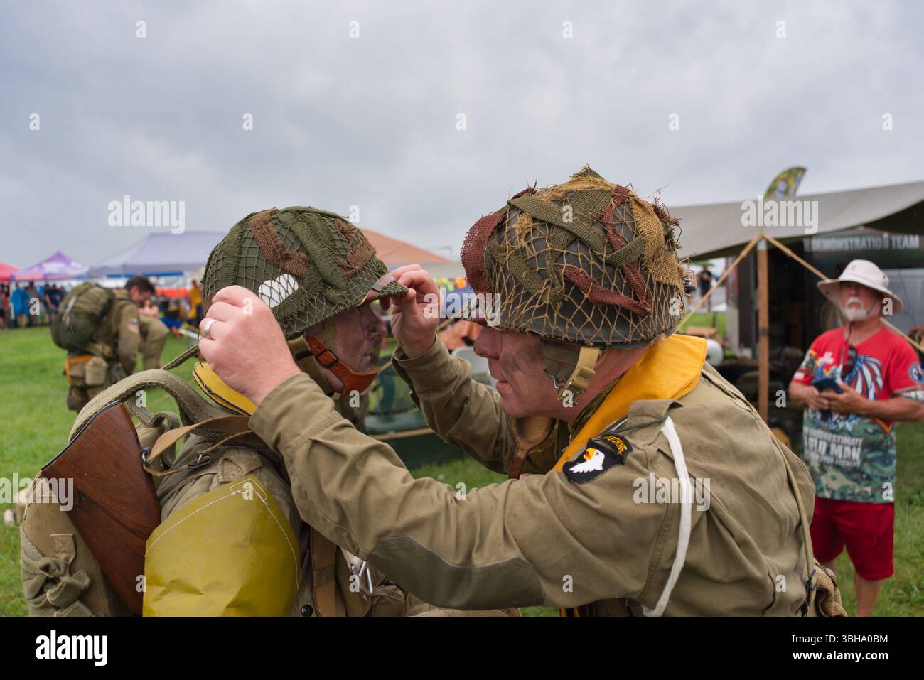 Two men in WWII-era US paratrooper helmets and uniforms are outdoors ...