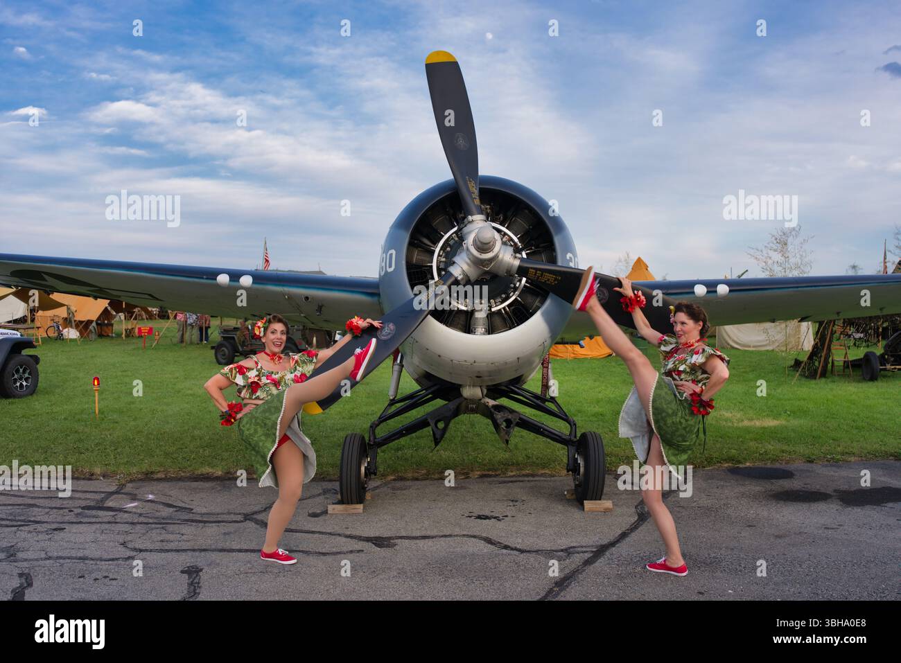Two women in vintage-style dresses perform a high leg kick against a ...