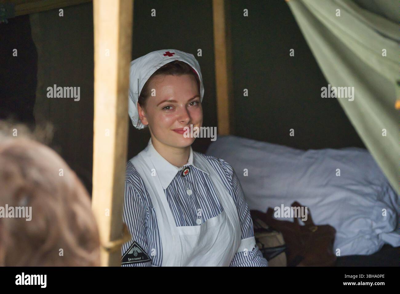 A young woman, dressed in a WWI-era nurse's uniform, smiles faintly ...