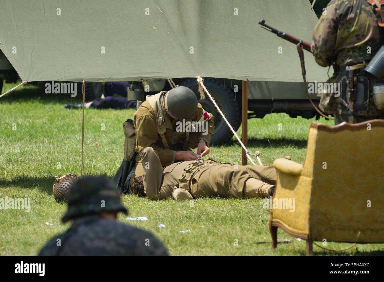 A medic in a WWII US Army uniform attends to a wounded soldier lying on ...