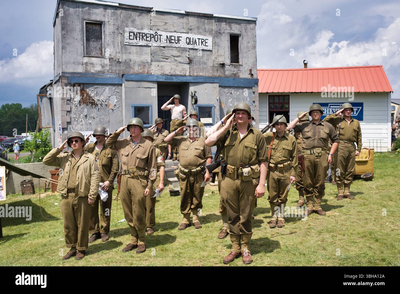 A group of men in WWII US Army reenactor uniforms salutes in front of a ...