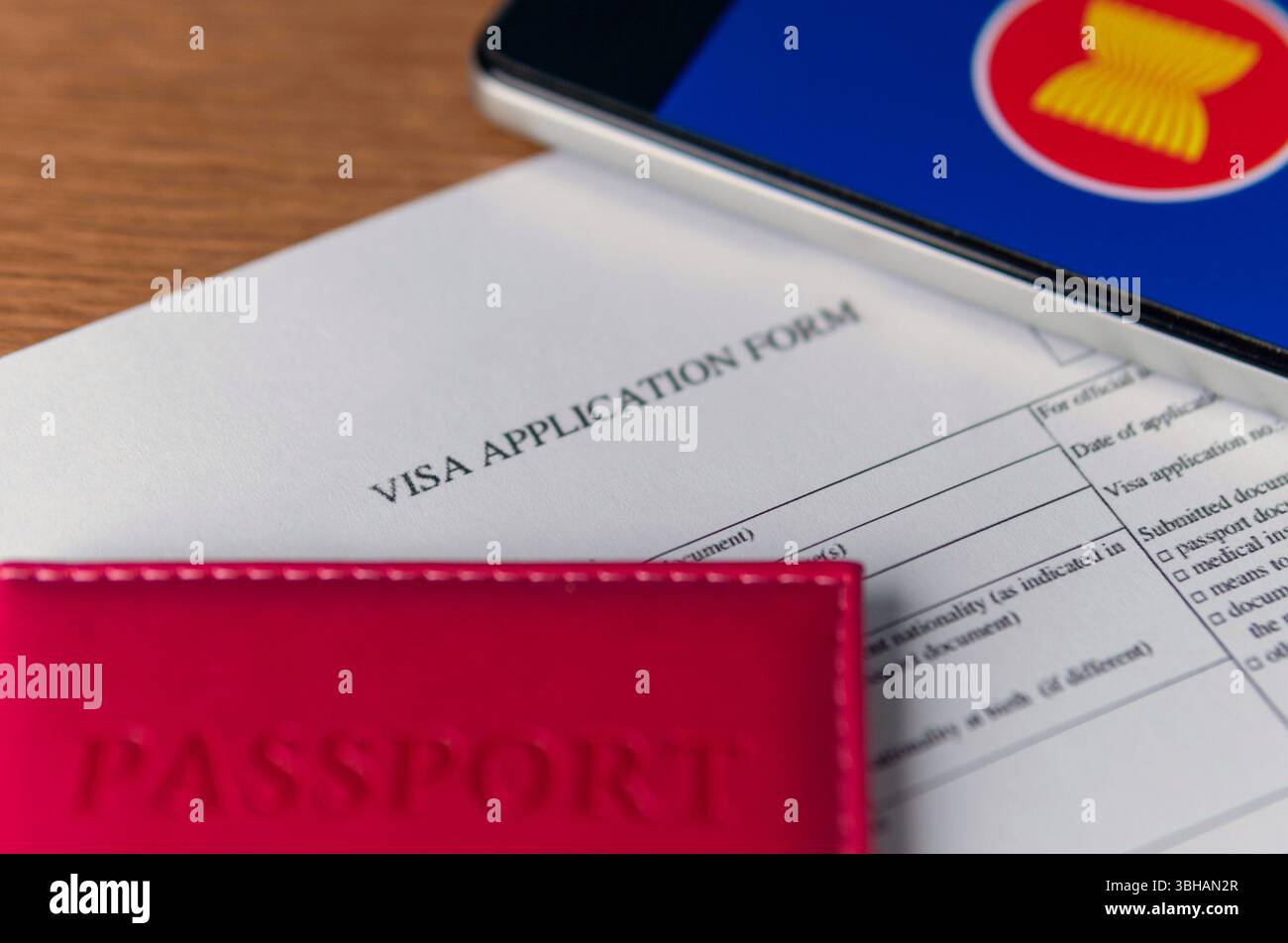 A passport, a visa application form, and a smartphone displaying the ASEAN flag on a wooden ...