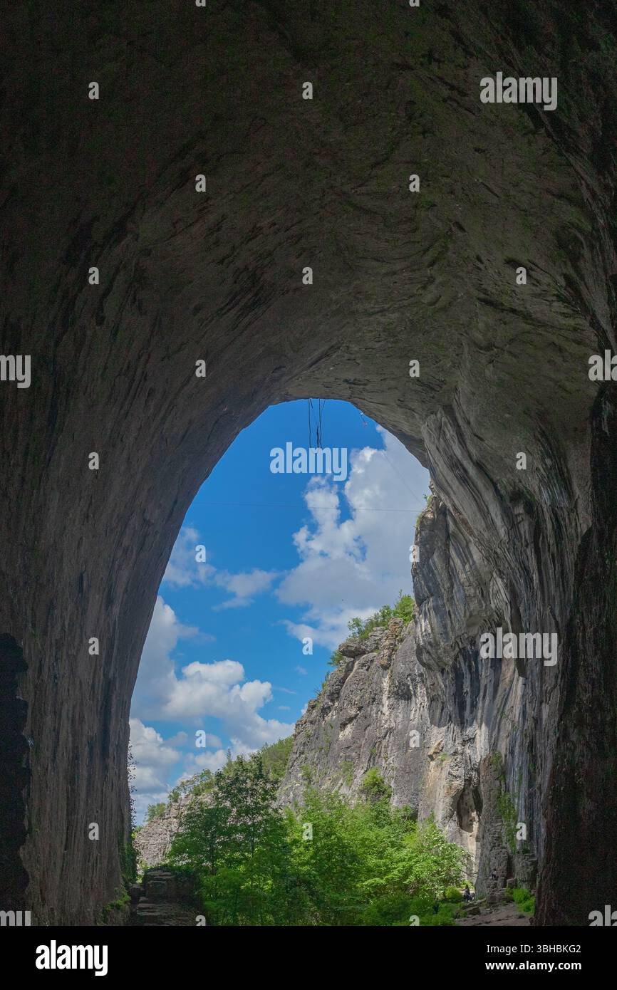 View from dark cave tunnel looking toward bright sky and steep rocky ...