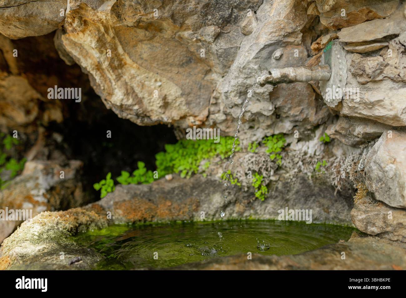 Water drops falling from weathered pipe into ancient mossy limestone ...