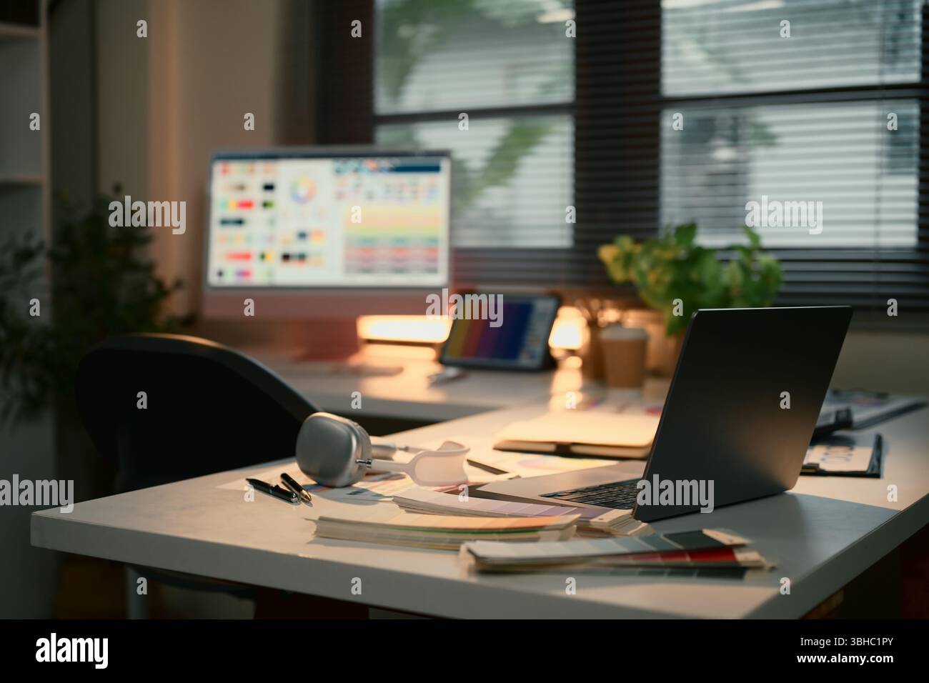 Modern graphic designer workspace with laptop, color swatches, and digital monitor showing color ...