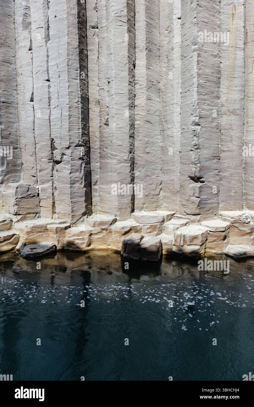 Majestic hexagonal basalt columns line the waters edge in Studlagil Canyon. The vibrant blue ...