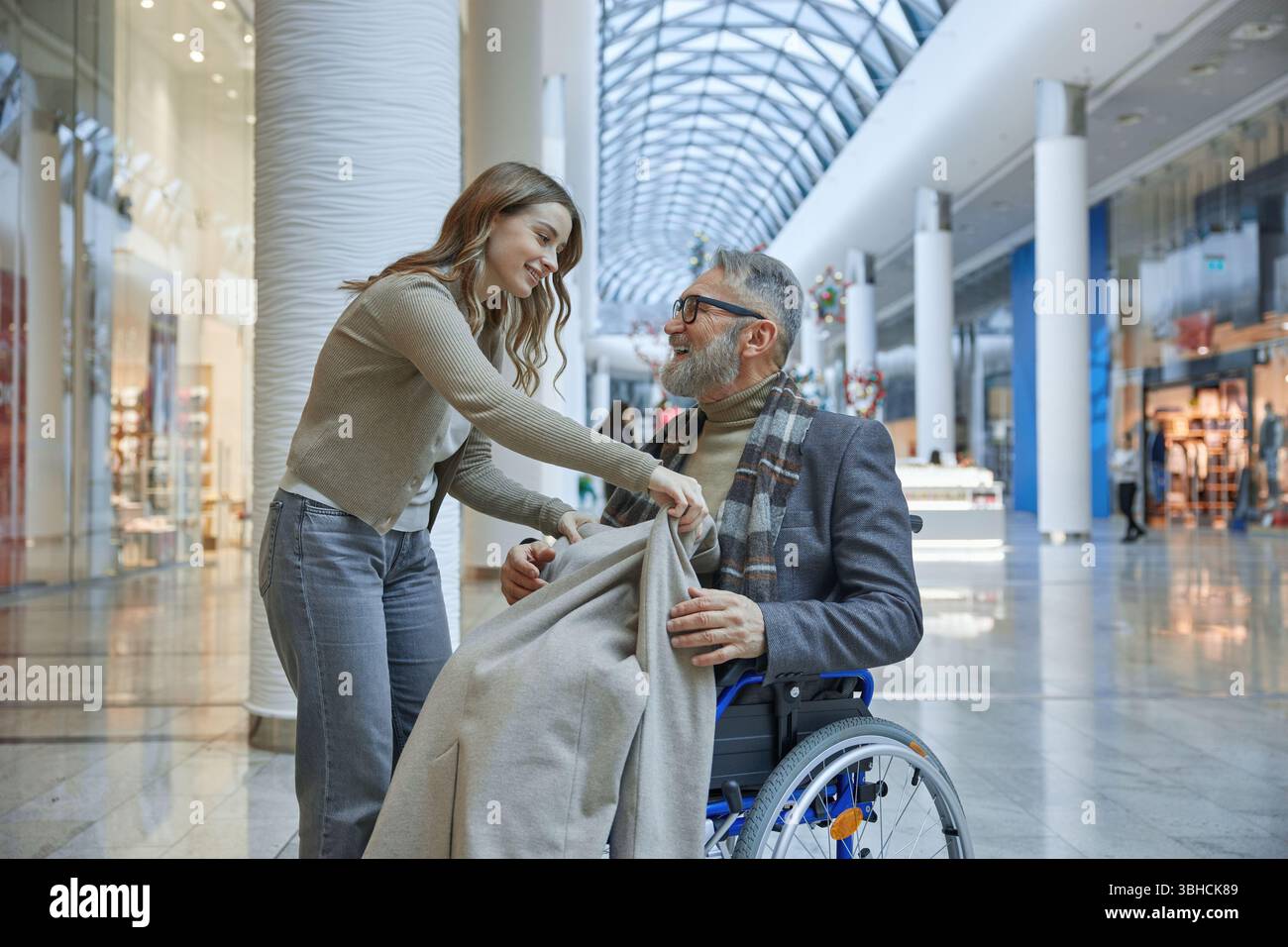 A woman is carefully placing a warm blanket over a man seated in a ...