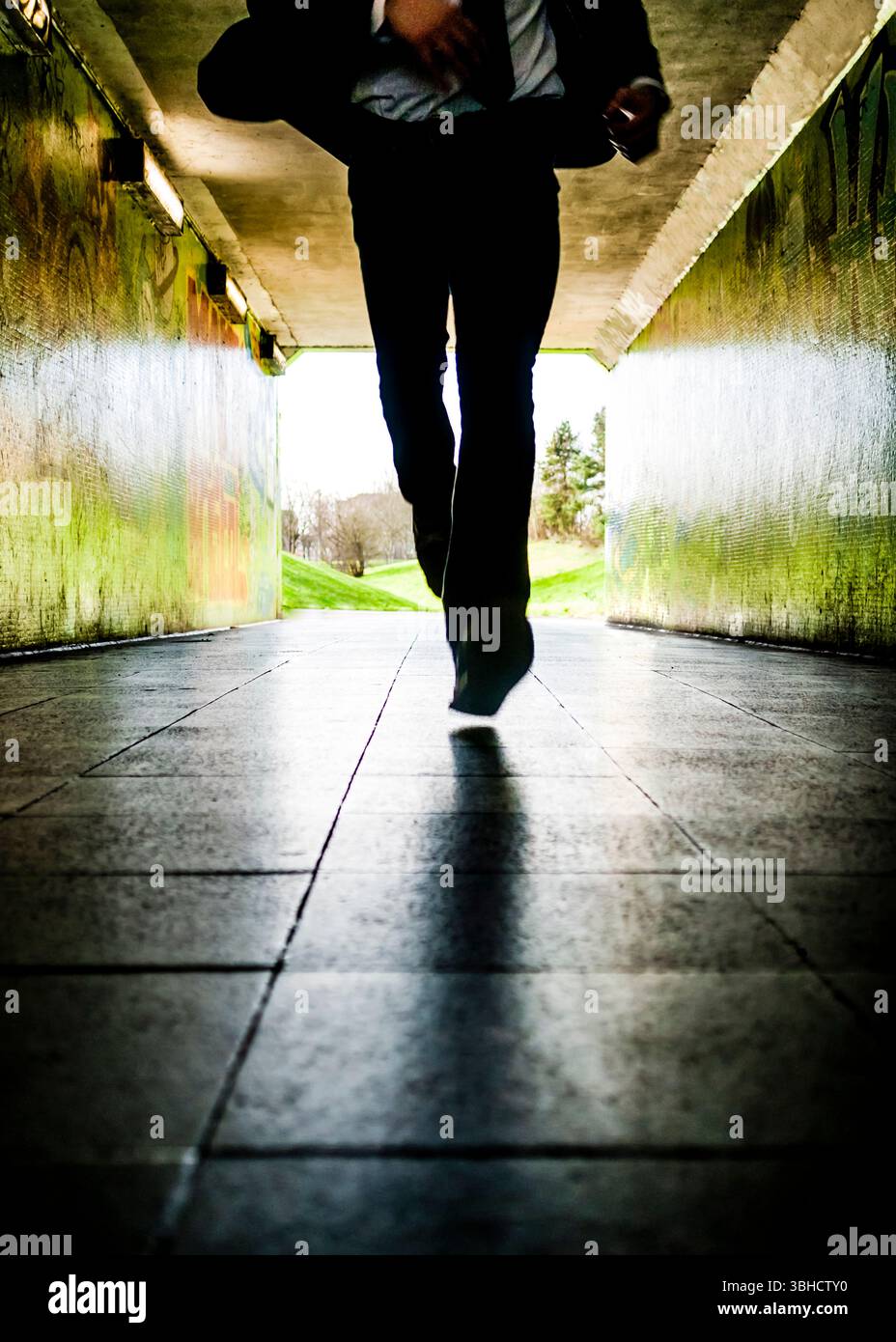A person wearing a suit is running through a pedestrian underpass. The ...