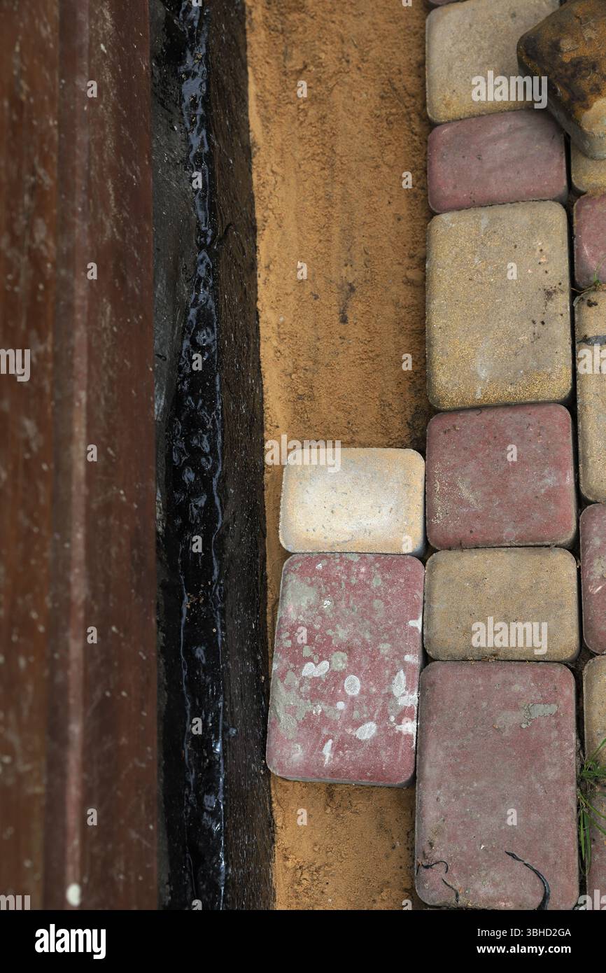 Paving stones laid on sand base near black waterproofed foundation. Urban yard construction ...