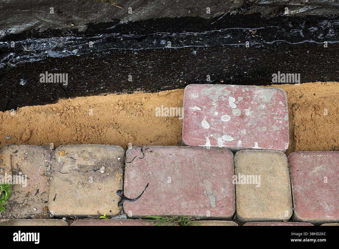 Paving stones laid on sand base near black waterproofed foundation. Urban yard construction ...