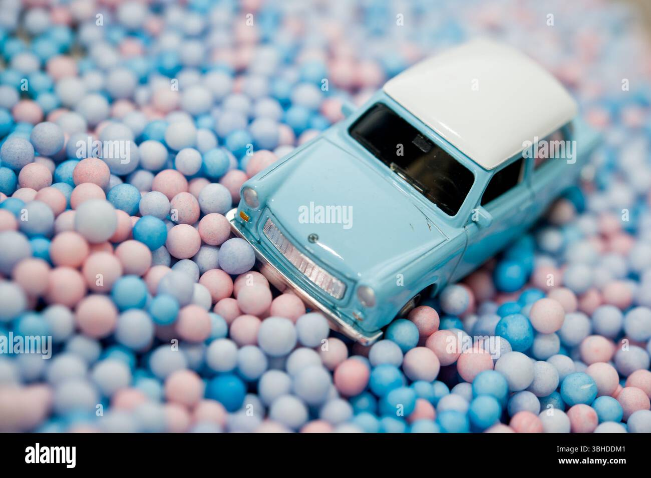 light blue toy car over a background of micro spheres in pastels colors ...