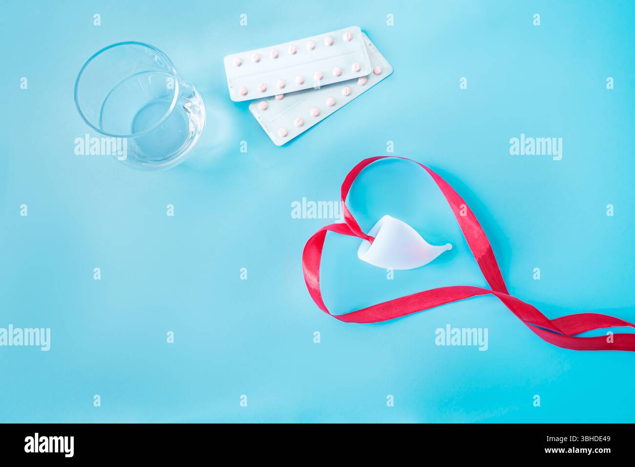 Menstrual cup inside red ribbon heart, with contraceptive pills and a ...