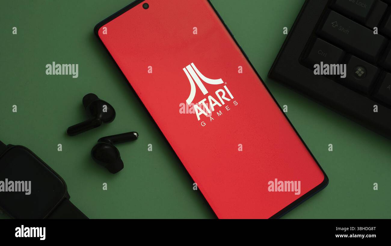 A smartphone displaying the Atari logo on a red screen, surrounded by ...