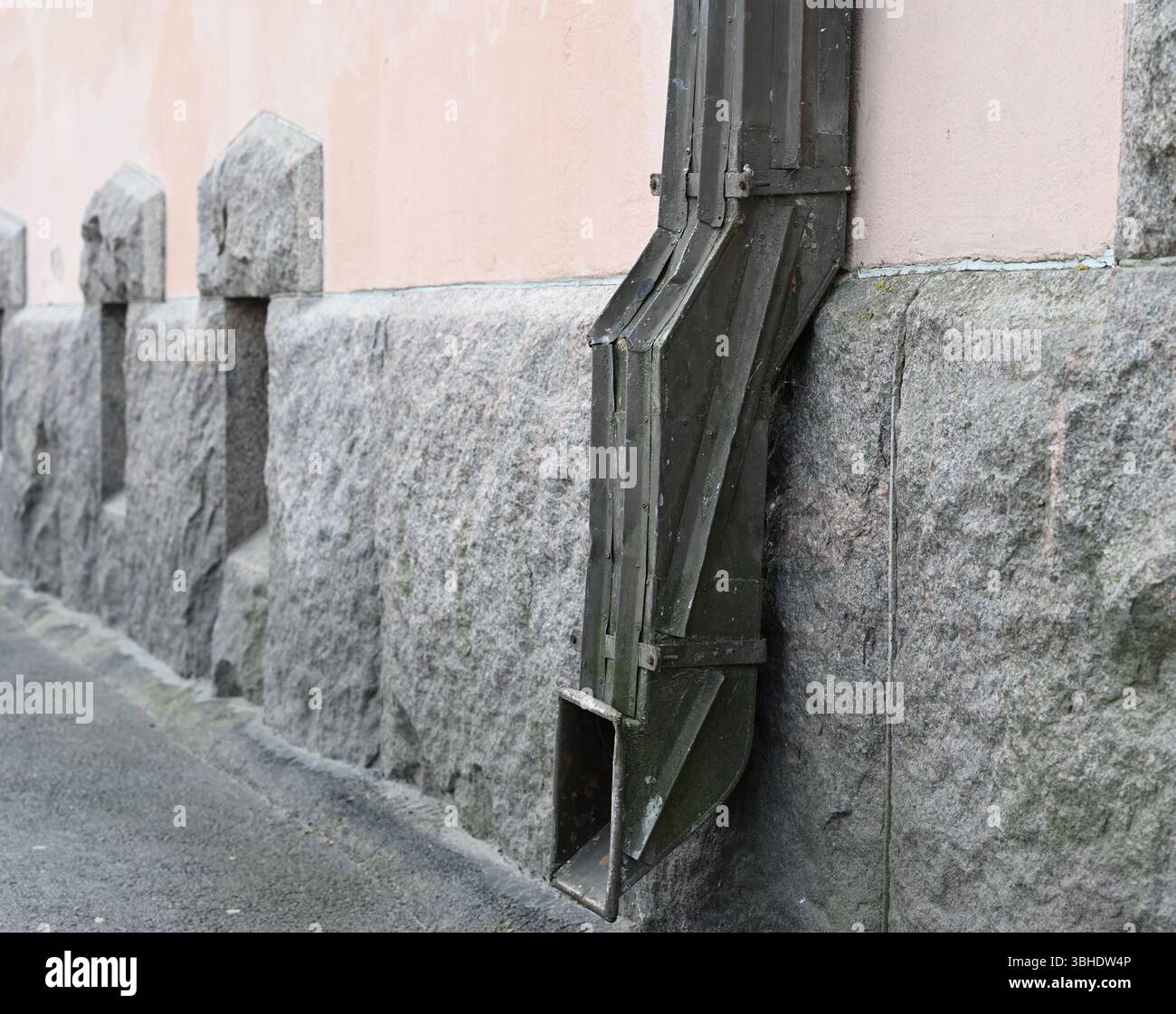 a close-up view of an aged metal rain gutter downspout attached to a ...