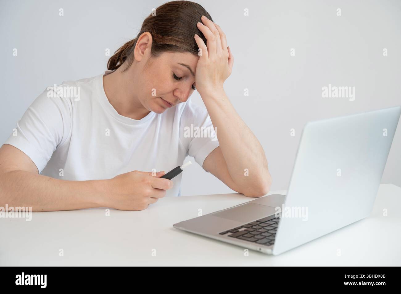 Tired woman smoking an electronic cigarette while working on a laptop ...