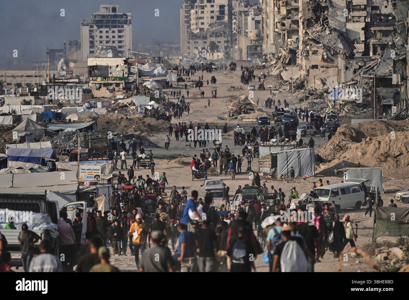 Displaced Palestinians walk past the ruins of destroyed buildings along ...