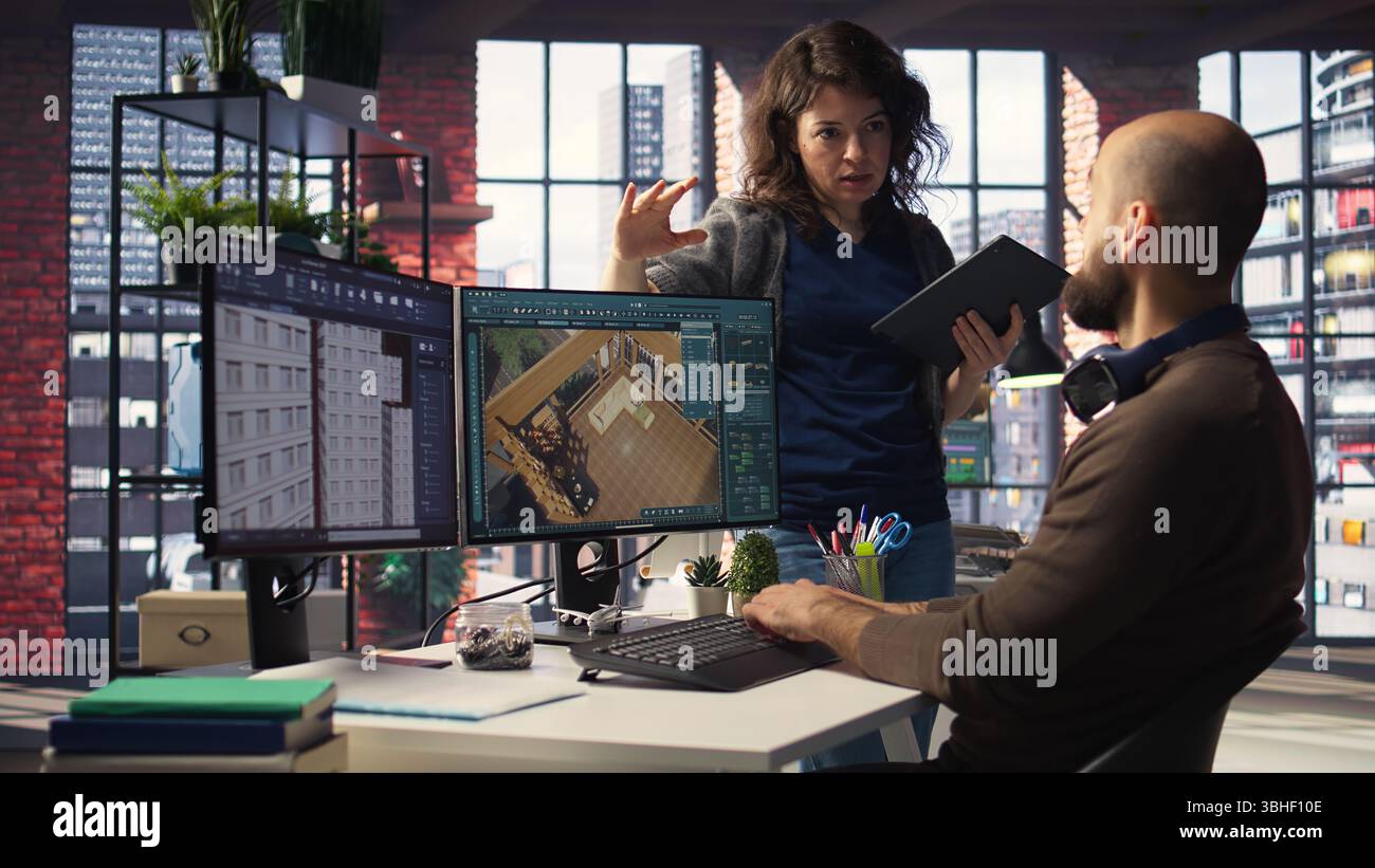 Architectural design team configures a floor plan on dual monitors, utilizing computer aided ...