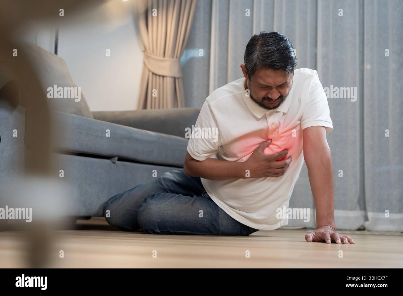 Middle-aged Asian man clutching his chest in pain while collapsing on ...