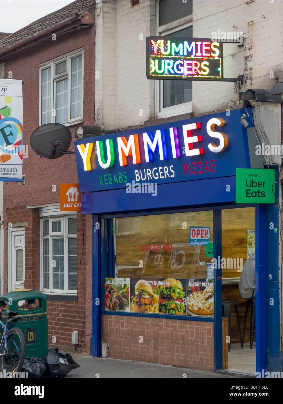 burger pizza kebab shop fast food outlet early evening neon signs lit ...