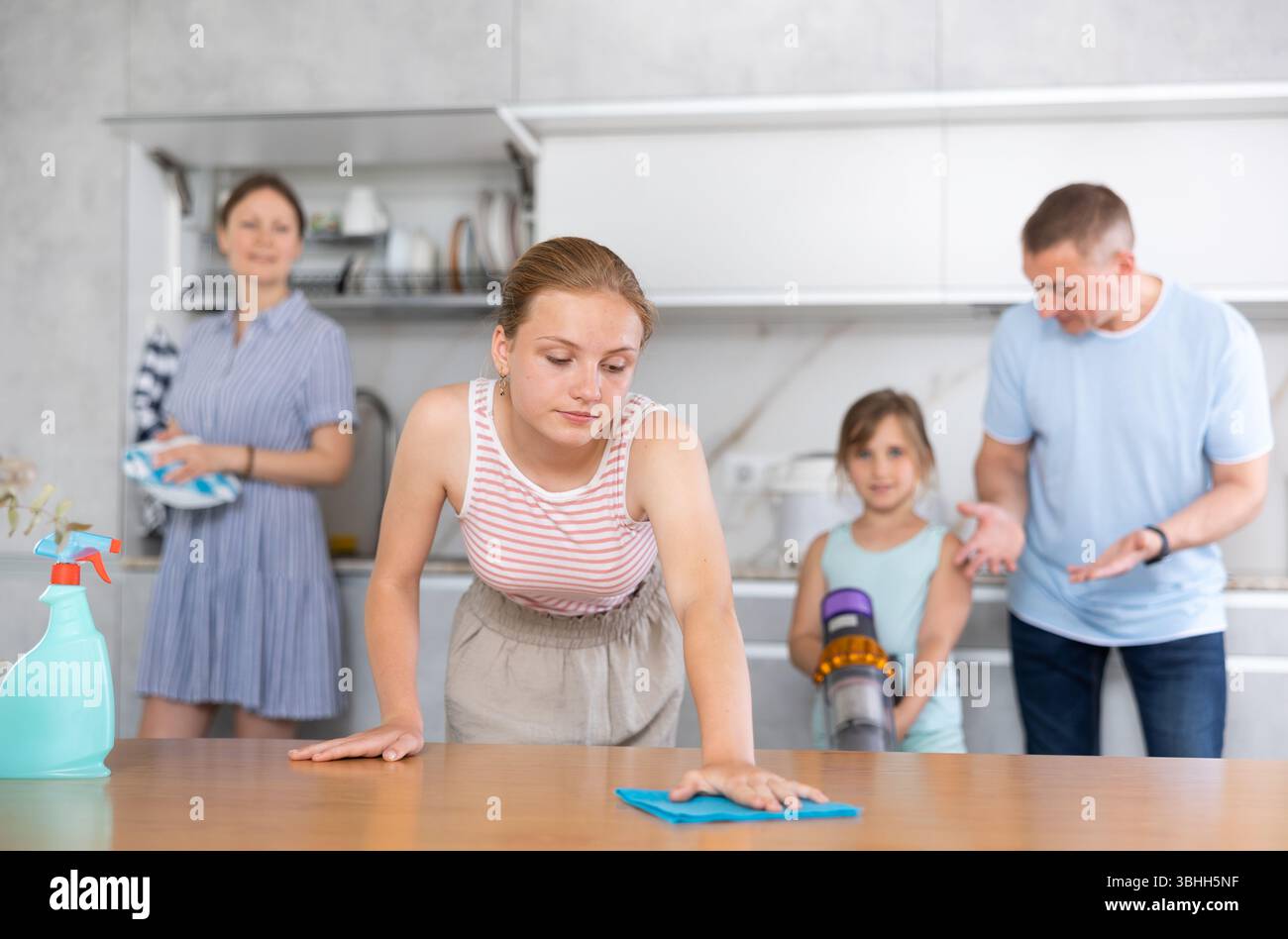 Teen girl cleans table with rag, family clean kitchen in background ...