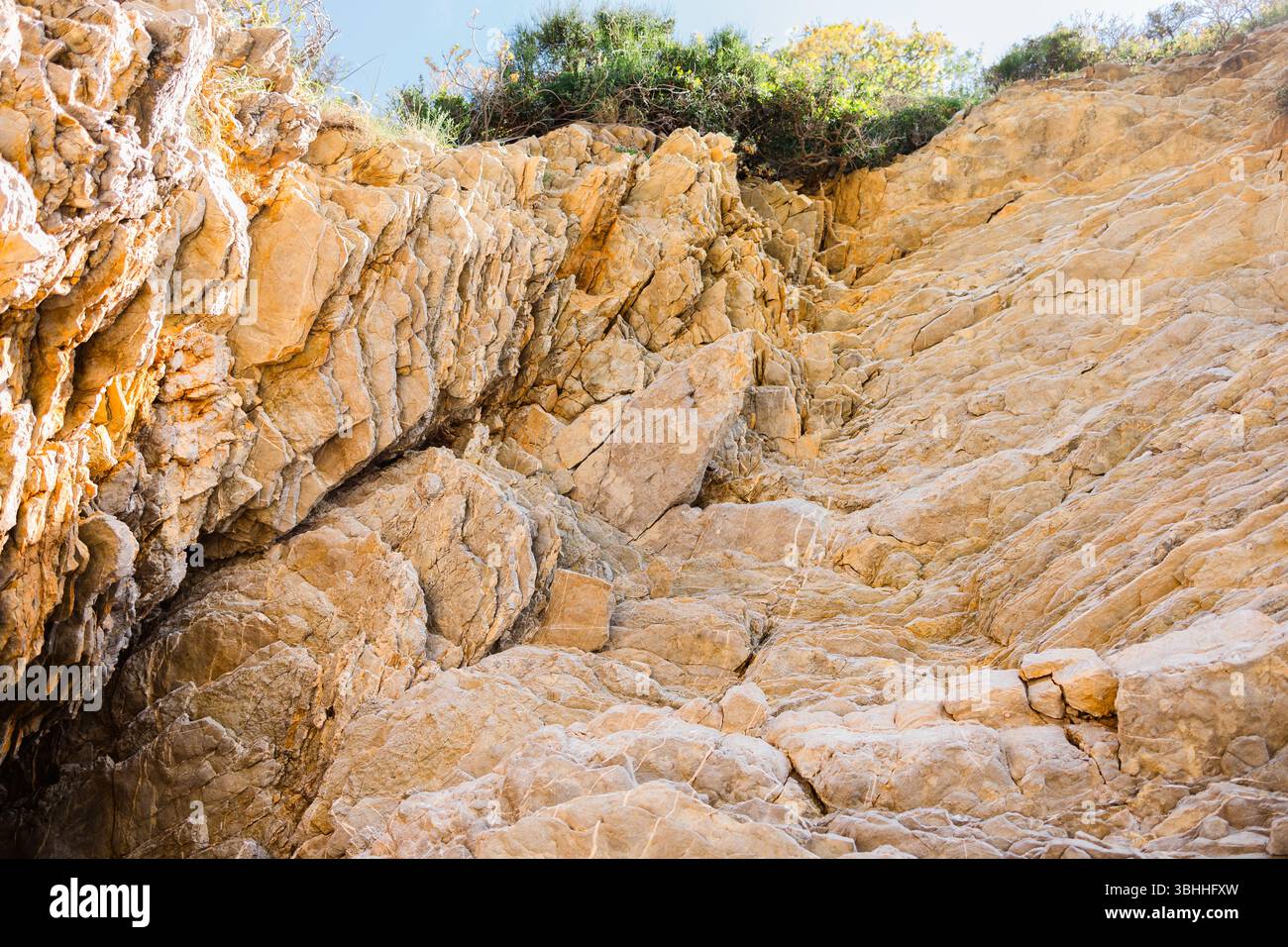 Sunlit rock wall with jagged natural lines and weathered surface ...