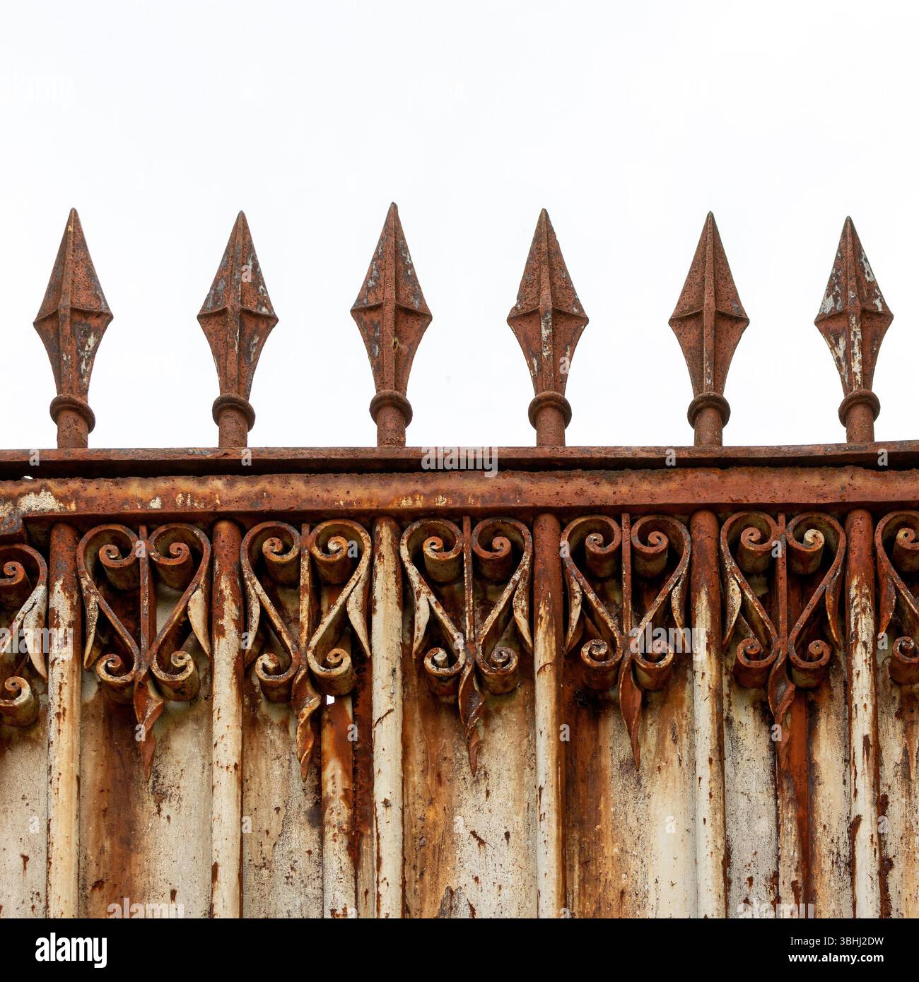 An old, weathered wrought iron fence features intricate scrollwork and ...