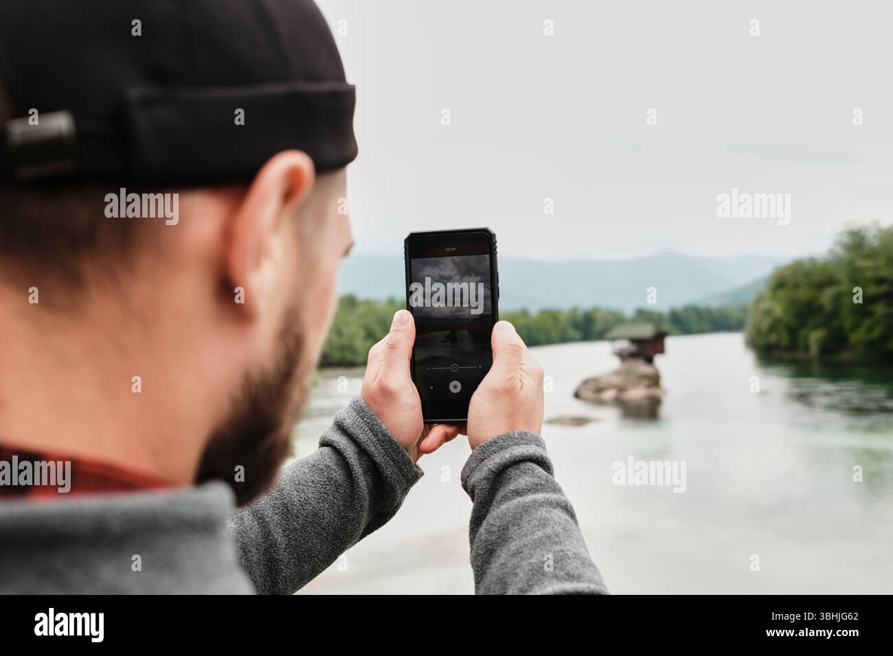 Close-up of a man filming the Drina River house on his phone, capturing ...