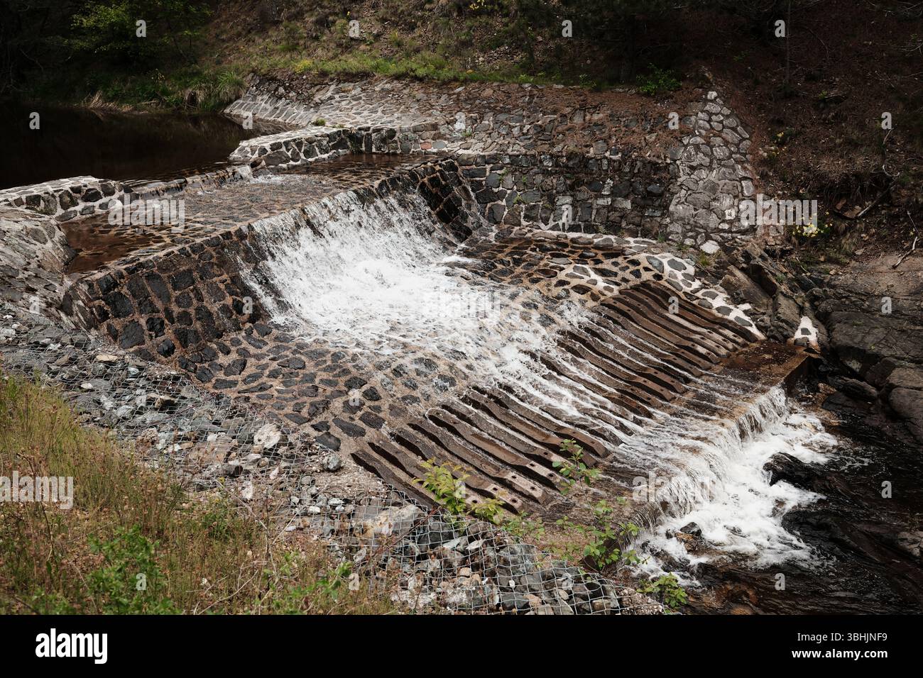 Wide stone dam with flowing water in Mokra Gora surrounded by forest ...