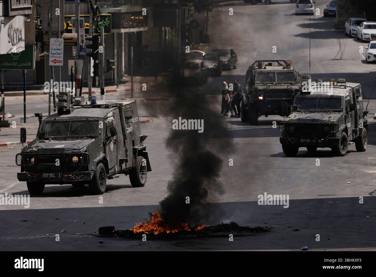 Israeli armoured vehicles drive past burning tires during a military ...