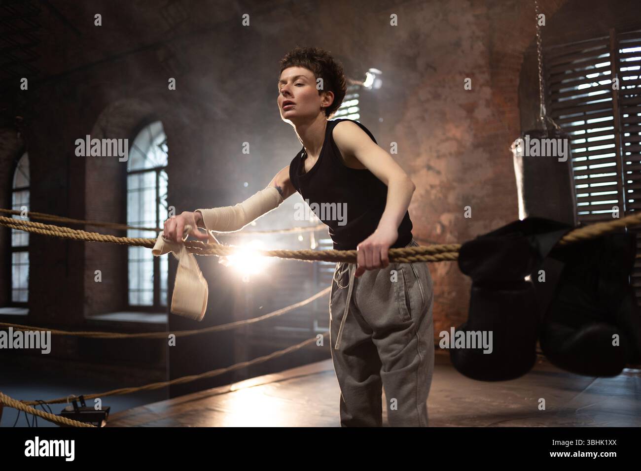 Boxer woman with short hair pausing on ropes, cinematic gym training ...