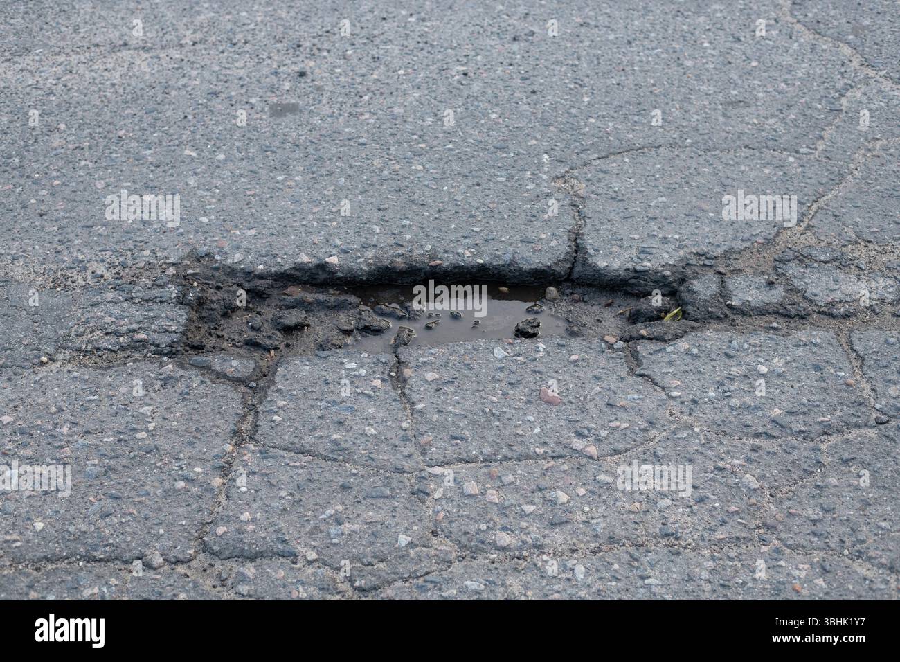 Large pothole on an asphalt road after rain. Cracks in the asphalt ...
