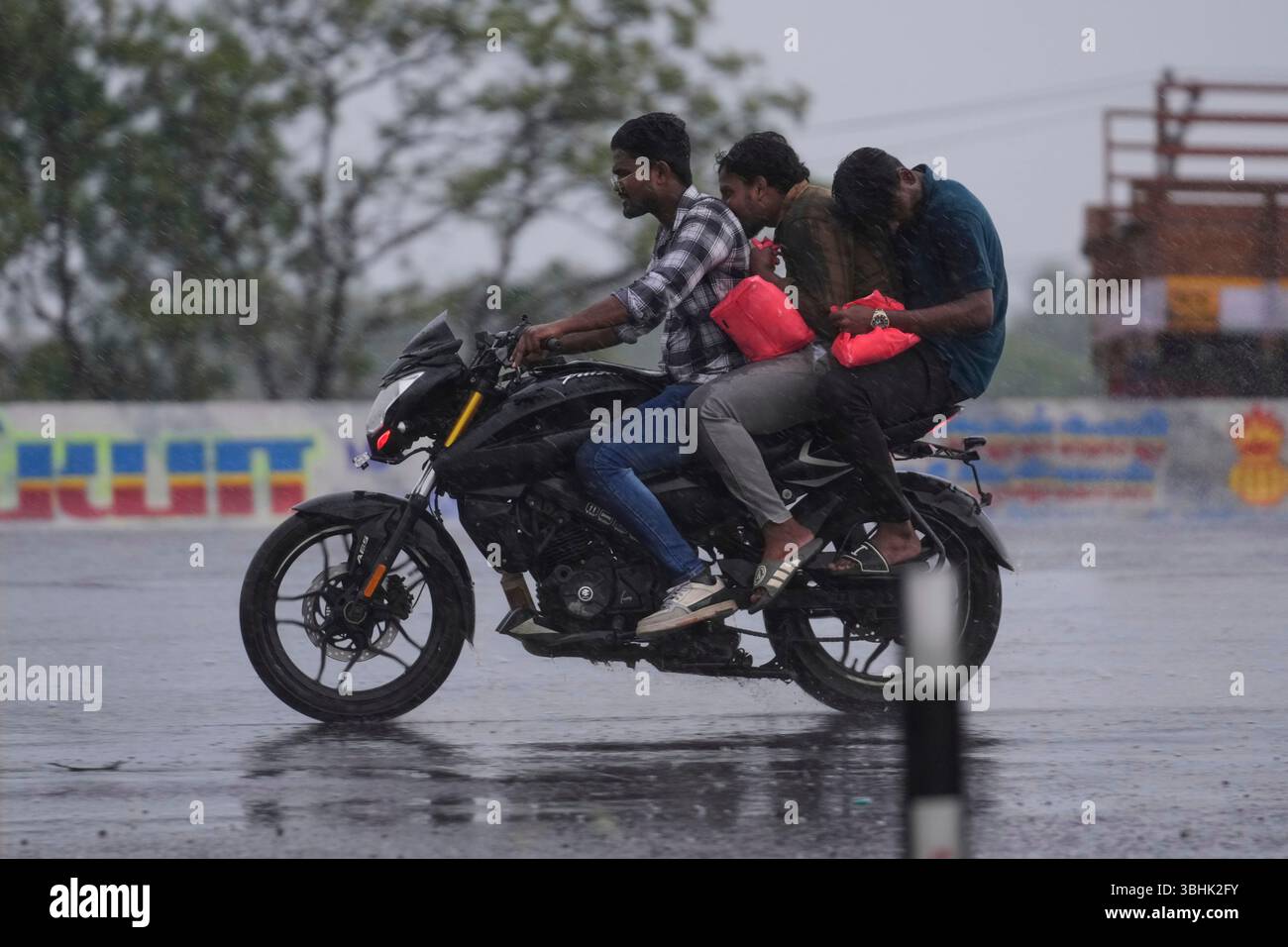 People rides on a bike as rain lashes down on them on the outskirts of ...
