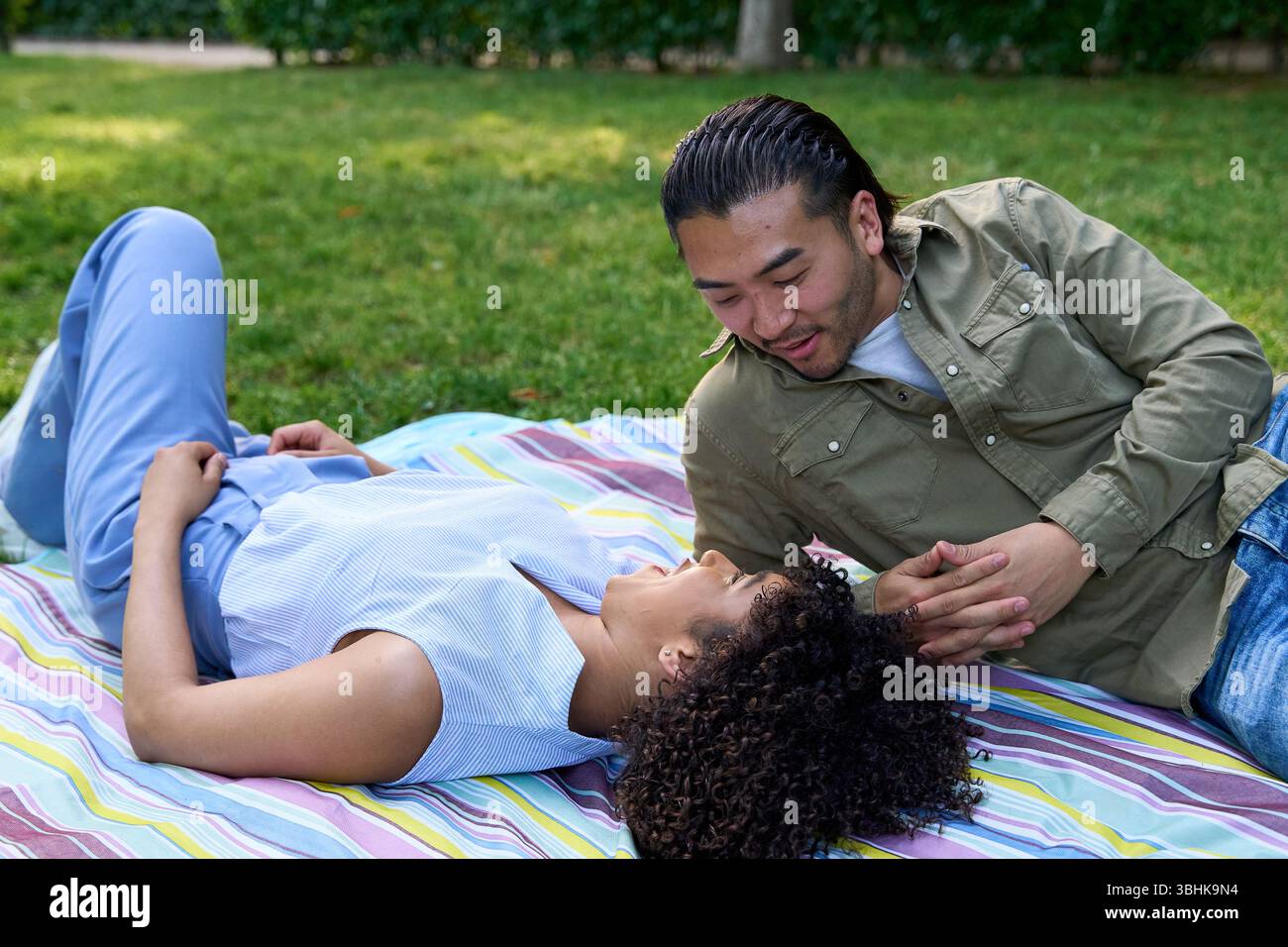 Interracial couple enjoying a romantic picnic in the park, lying on a colorful blanket and ...